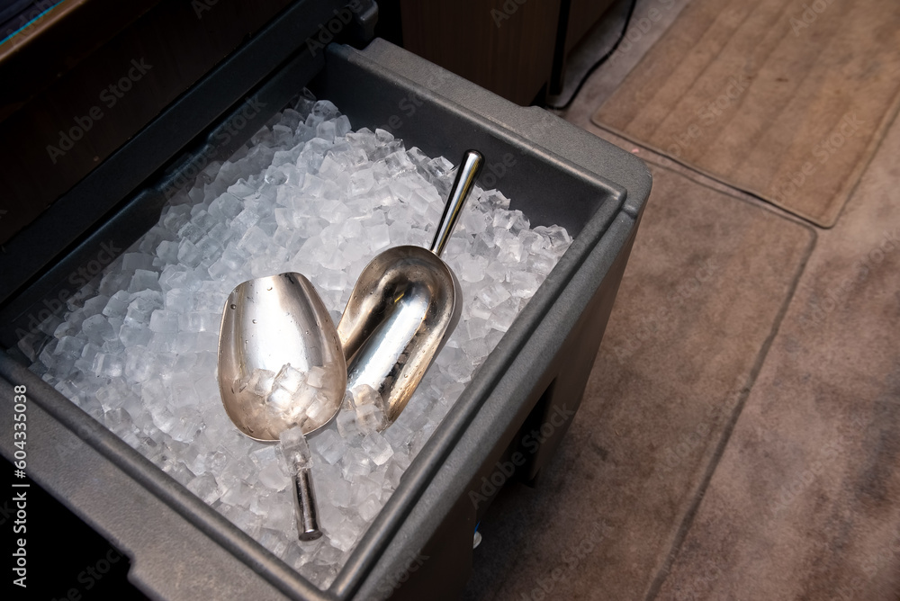 Photograph of two ice scoops lying on top of a pile of white ice. The ...