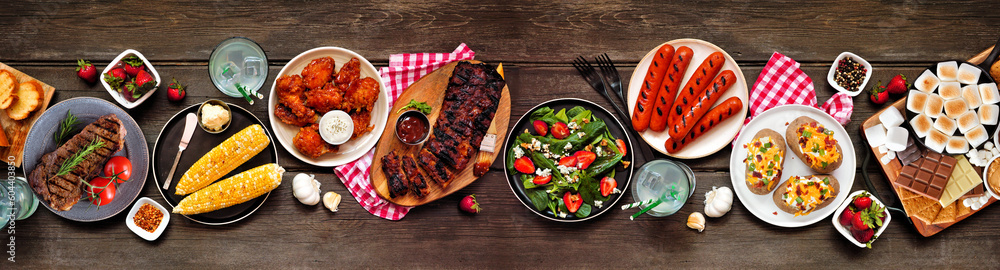 Summer BBQ food table scene over a dark wood banner background ...