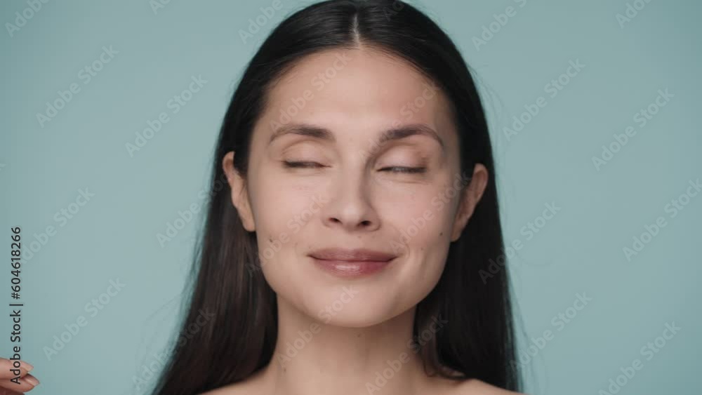 A young woman runs her manicured hand over her chin and turns her face ...