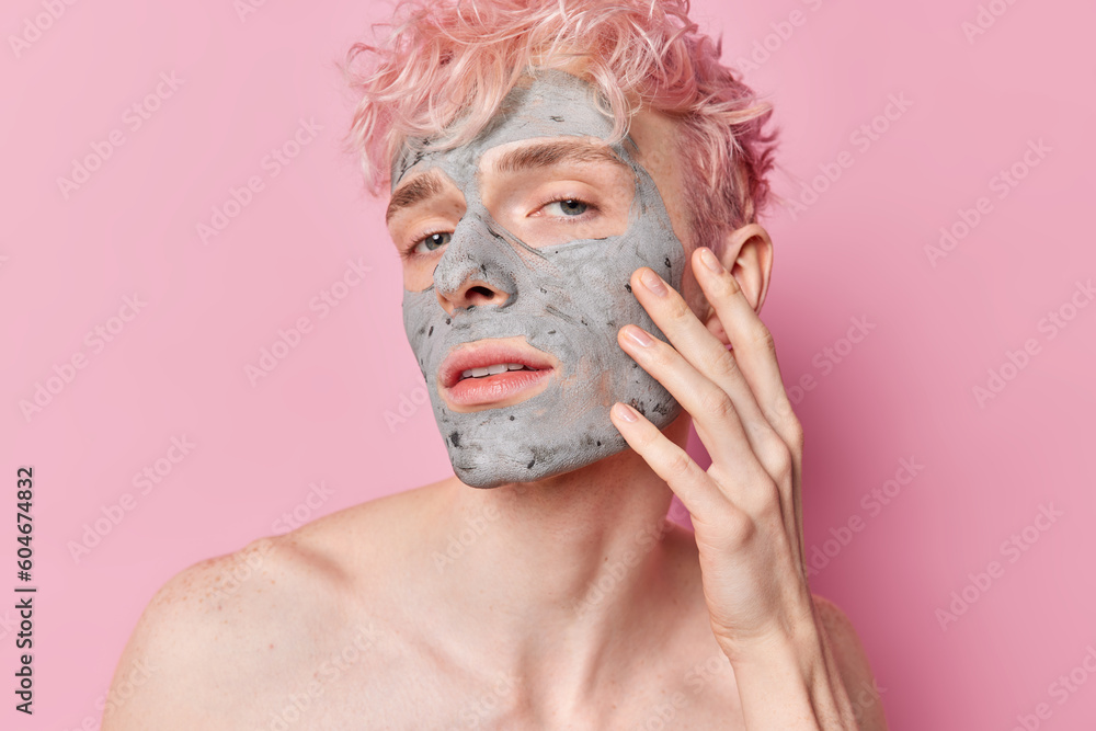 Serious pink haired guy examines condition of facial skin applies ...