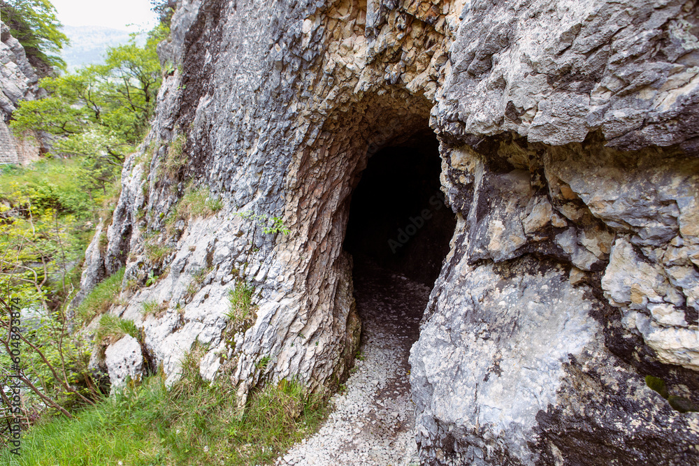 Rock wall with a dark hole, entrance to the cave in Jura mountains ...