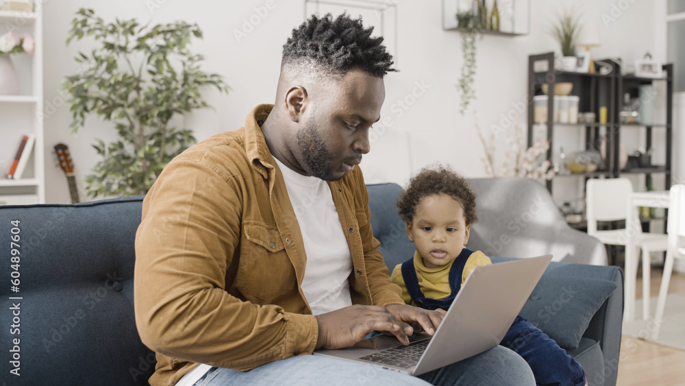 Working father types on his laptop while watching his cute little son ...