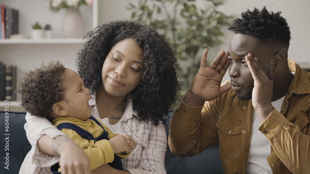 Father making funny faces to cheer up crying baby sitting on mom's lap ...