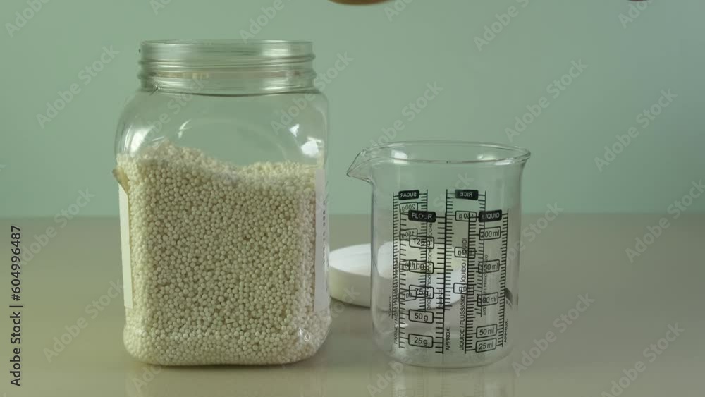 Tapioca pearls or white sago balls are poured with spoon into measuring ...