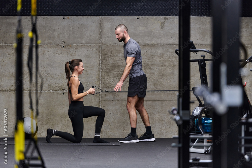 A muscular man assisting a fit woman in a modern gym as they engage in ...