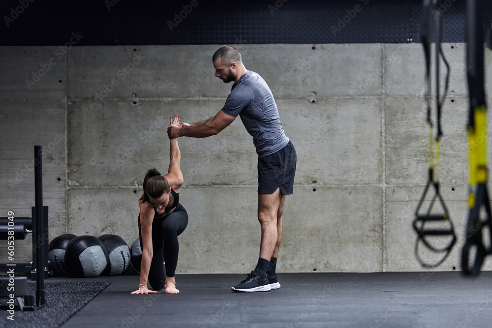 A muscular man assisting a fit woman in a modern gym as they engage in ...