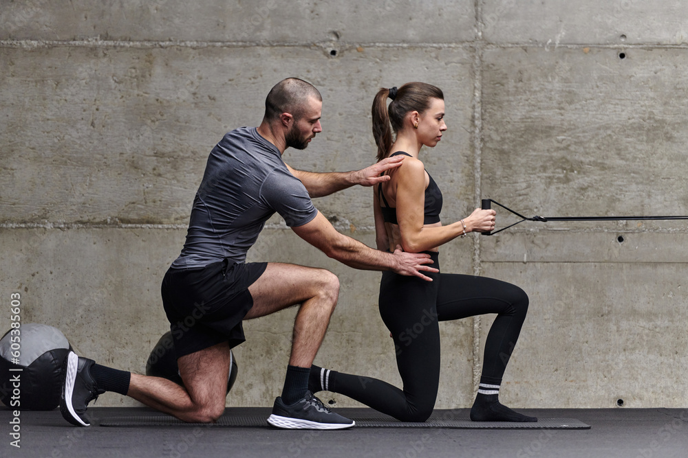 A muscular man assisting a fit woman in a modern gym as they engage in ...