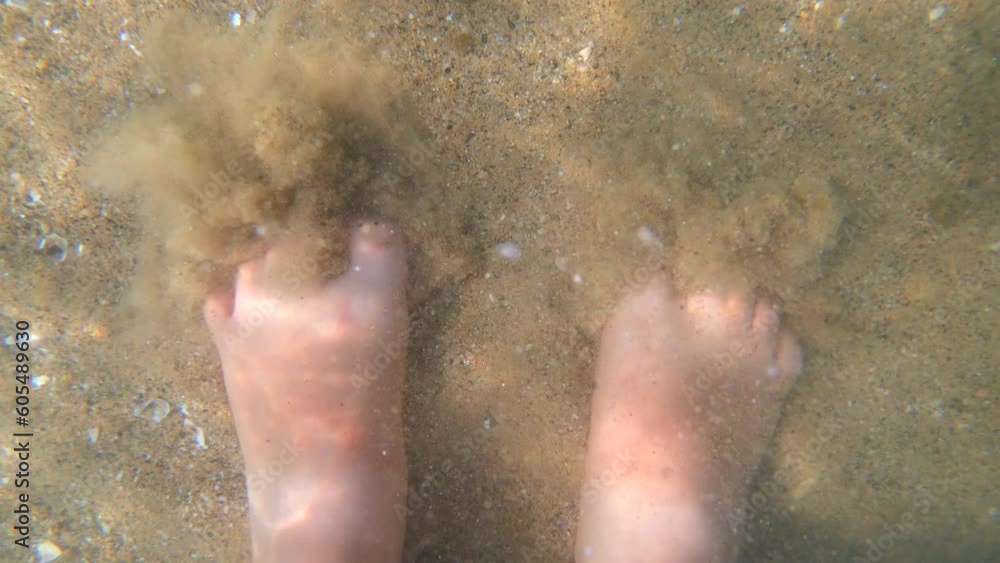 Woman standing barefoot on sand underwater and digging her feet into sand. Woman digging her ...