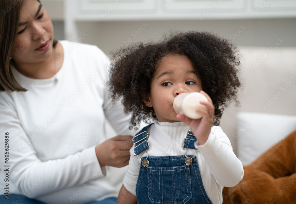 Cute biracial little girl sucking milk from bottle. Asian mother take ...