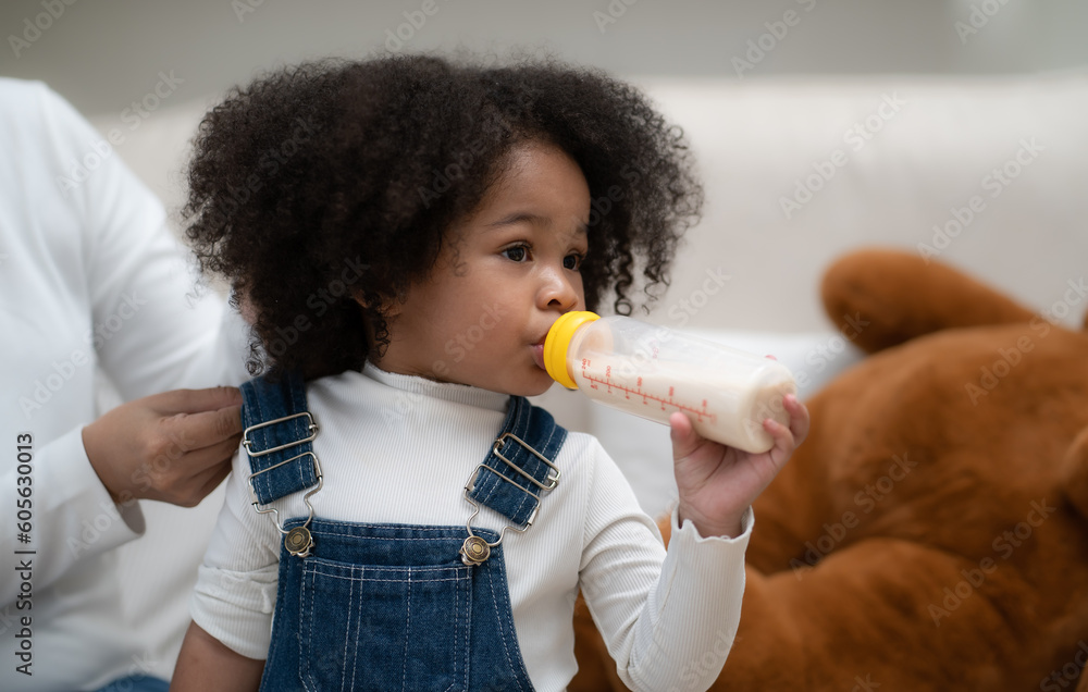 Cute curly hair biracial little girl sucking milk from bottle. Hungry ...