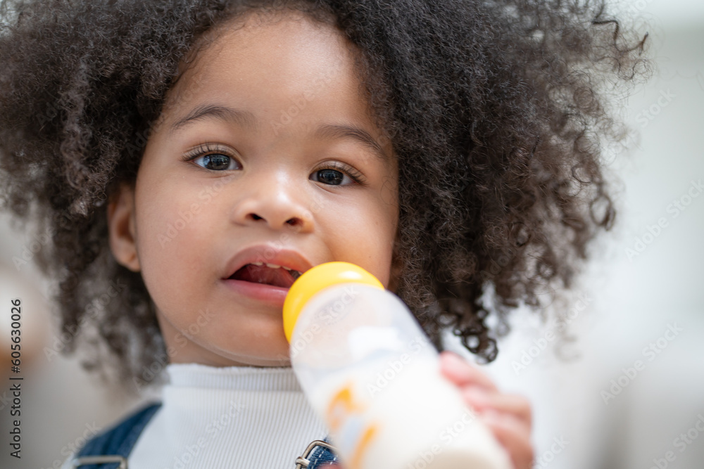 Cute curly hair biracial little girl sucking milk from bottle. Hungry ...