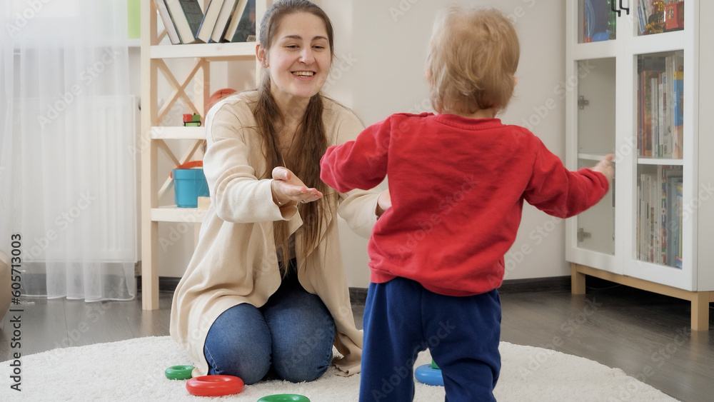 Happy smiling mother looking and helping her little baby boy making his ...