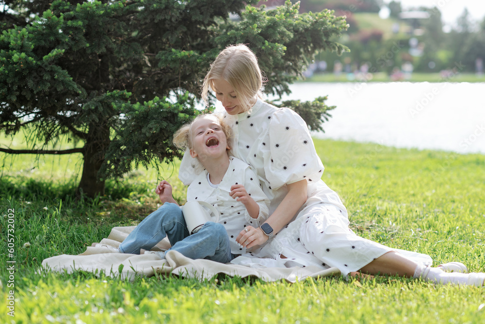 Blond young mother with disabled daughter sitting ot the green grass in ...