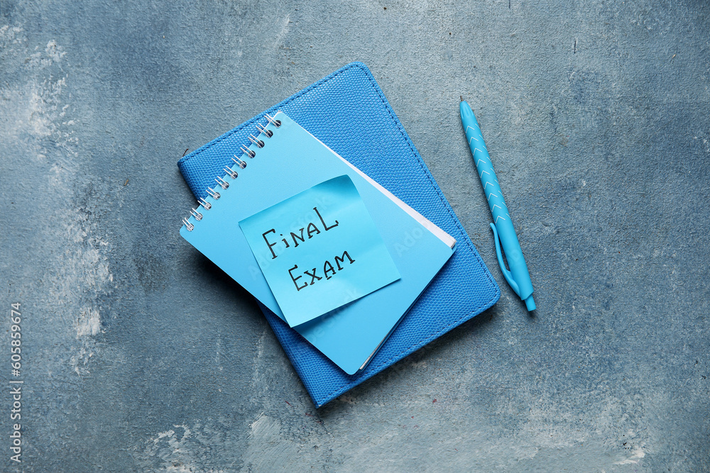 Sticky note with text FINAL EXAM, notebooks and pen on grunge blue ...