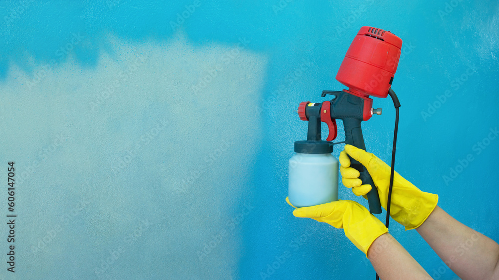 A worker's hands in yellow gloves hold a hand-held spray gun with an ...