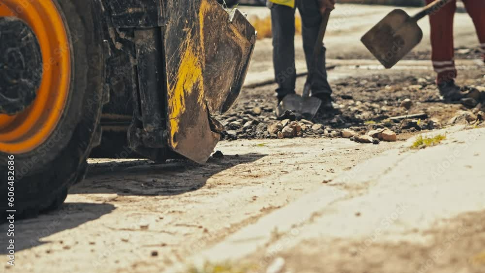 shovel construction debris into the excavator bucket. Road workers ...