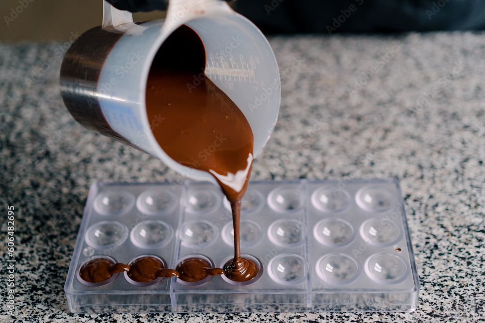 Pouring chocolate into molds in a professional kitchen tempering ...