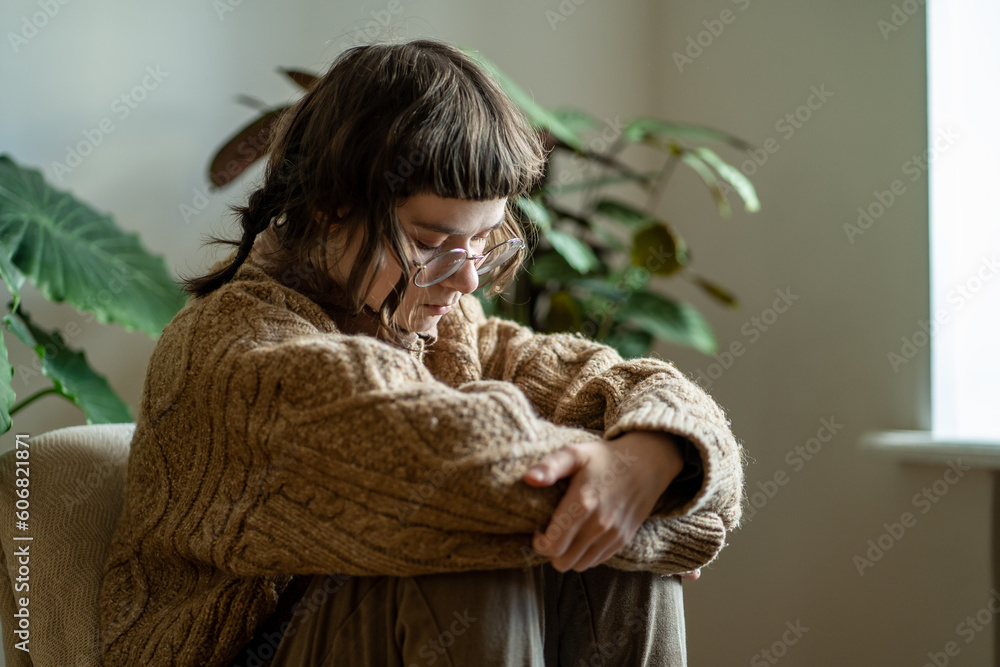 Sad millennial girl artist sitting on chair by window feeling lack of ...