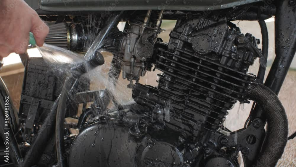 Man washes custom motorcycle engine with a hose. The follow shot shows ...
