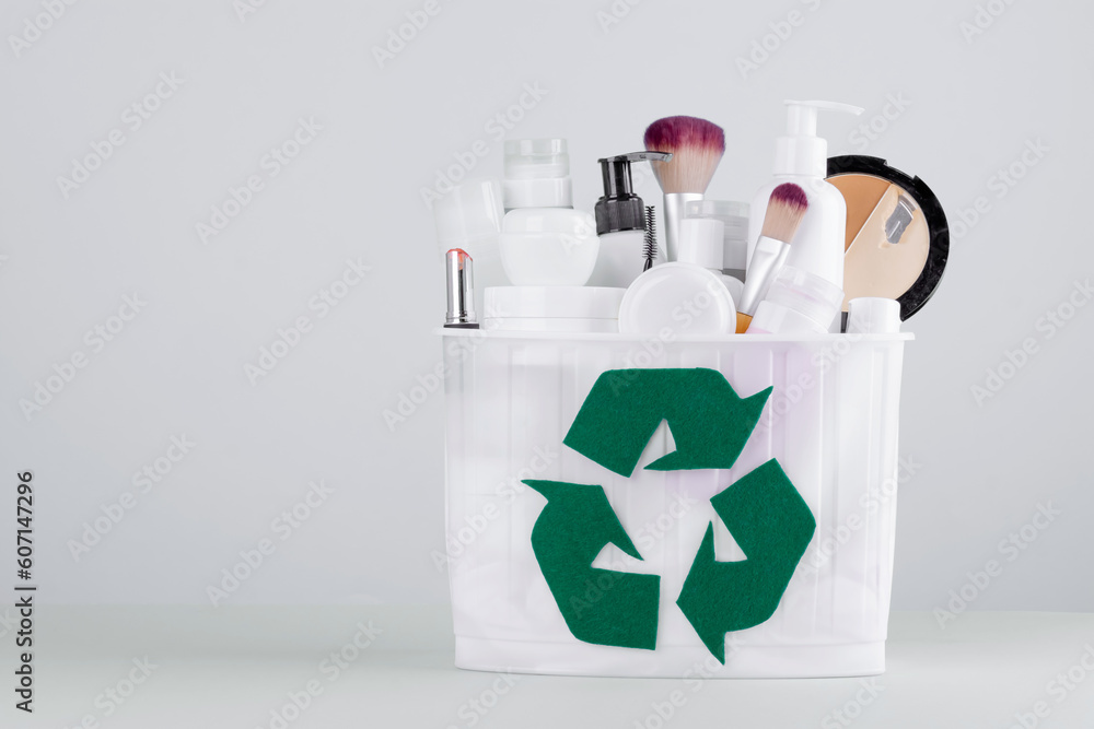 A container full of cosmetic products with a recycling sign on a gray ...
