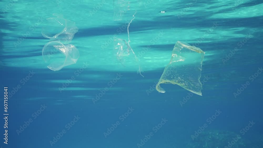 Close-up of plastic debris drifts under surface in blue water, Slow ...