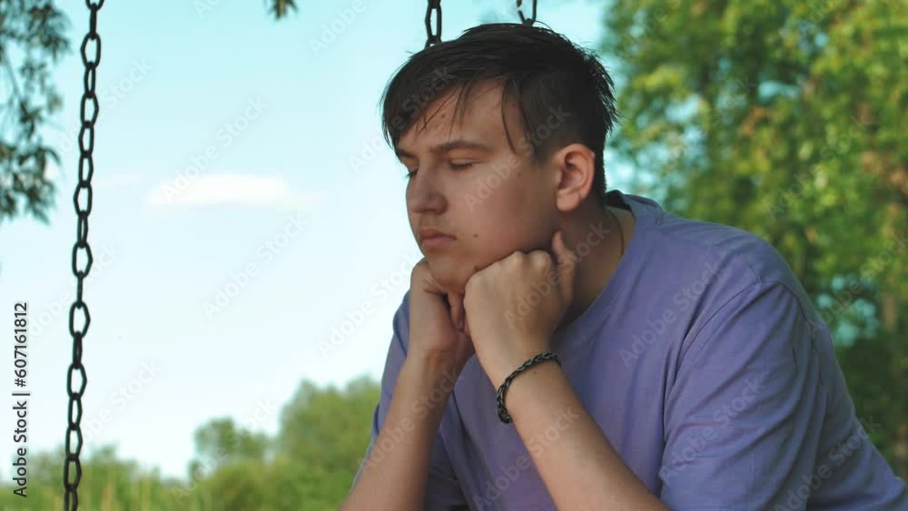 Guy is sitting on the swing in a depressed state. Close-up face of sad ...