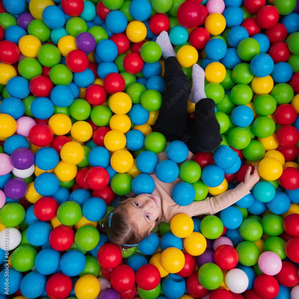 Cute little girl playing on multi coloured plastic balls in big dry ...
