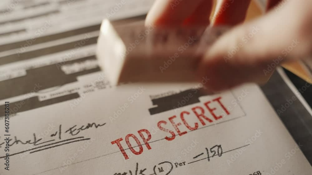 Close up hand marks classified document as Top Secret with red ink ...