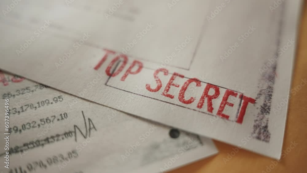 Classified official looking paper with Top Secret red stamp is laid on desk. Close up on the red ...