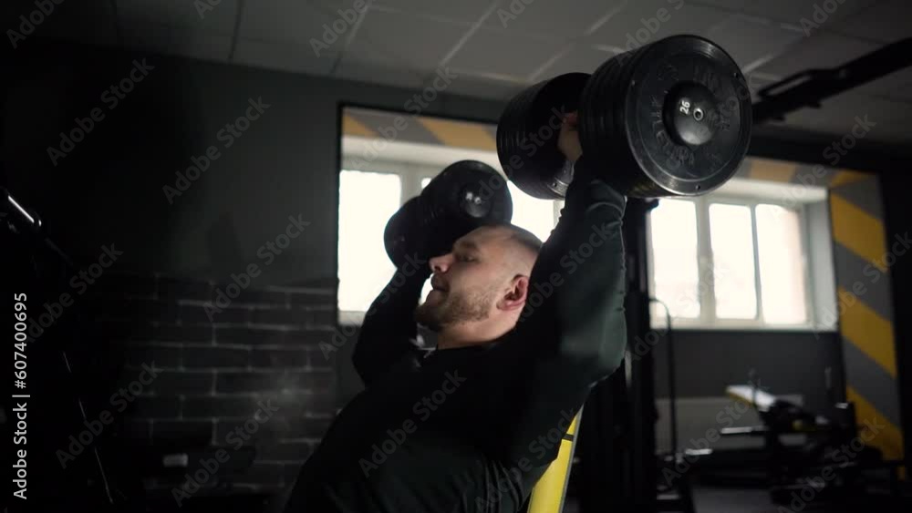 A strong male bodybuilder shakes his biceps in the gym with a barbell ...