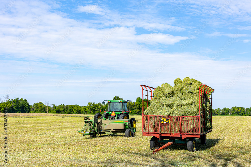A John Deere tractor and small square baler next to an H&S hay wagon ...