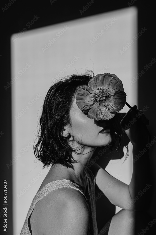 Woman hiding face by poppy flower over wall with sun light shades ...