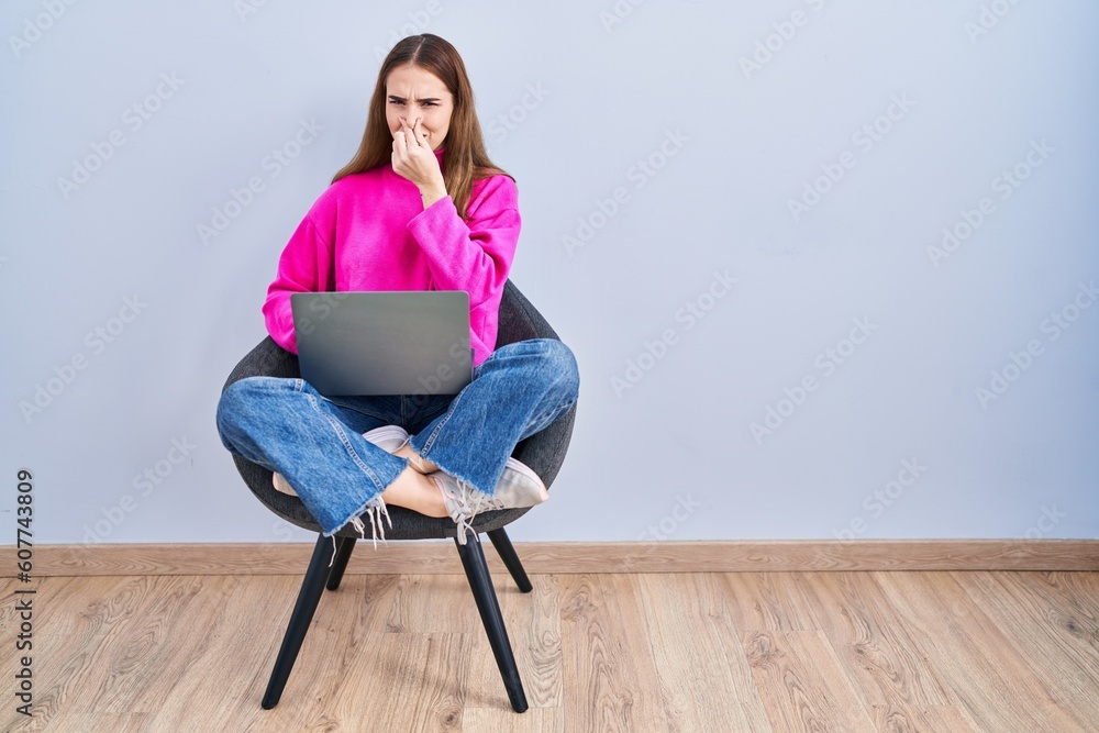 Young hispanic girl working using computer laptop smelling something ...