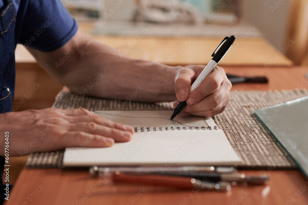 Glass worker drawing wavy line in notepad when working on sketches for ...