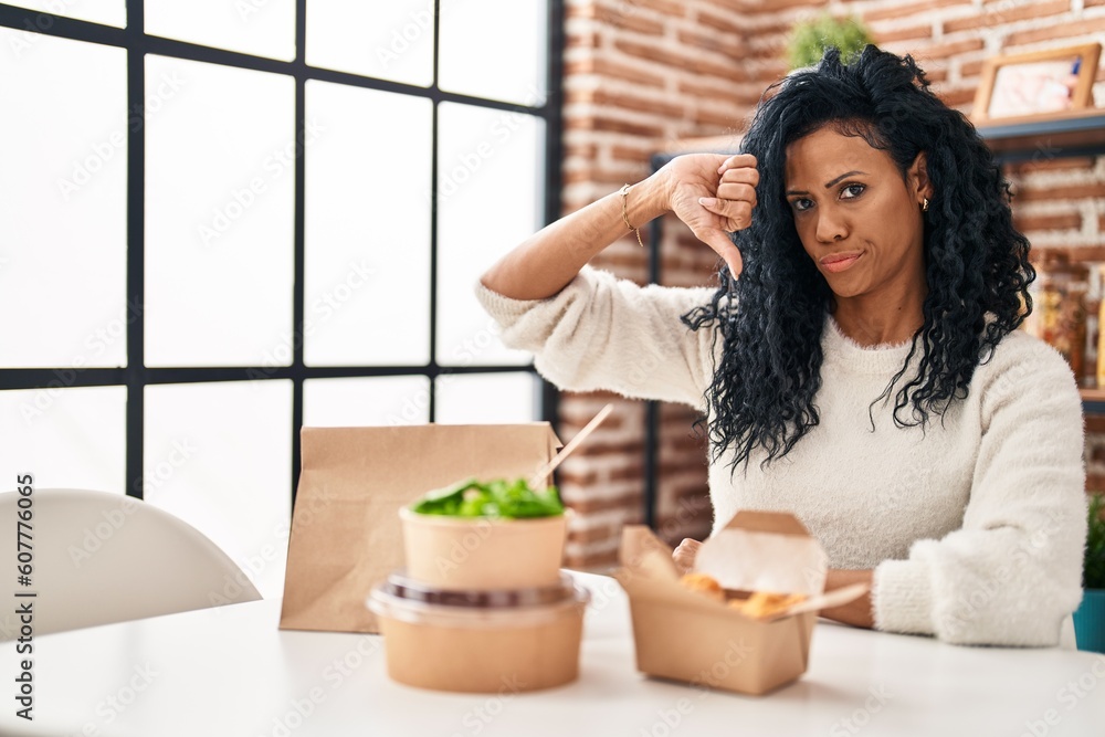 Middle age hispanic woman eating take away food with angry face ...