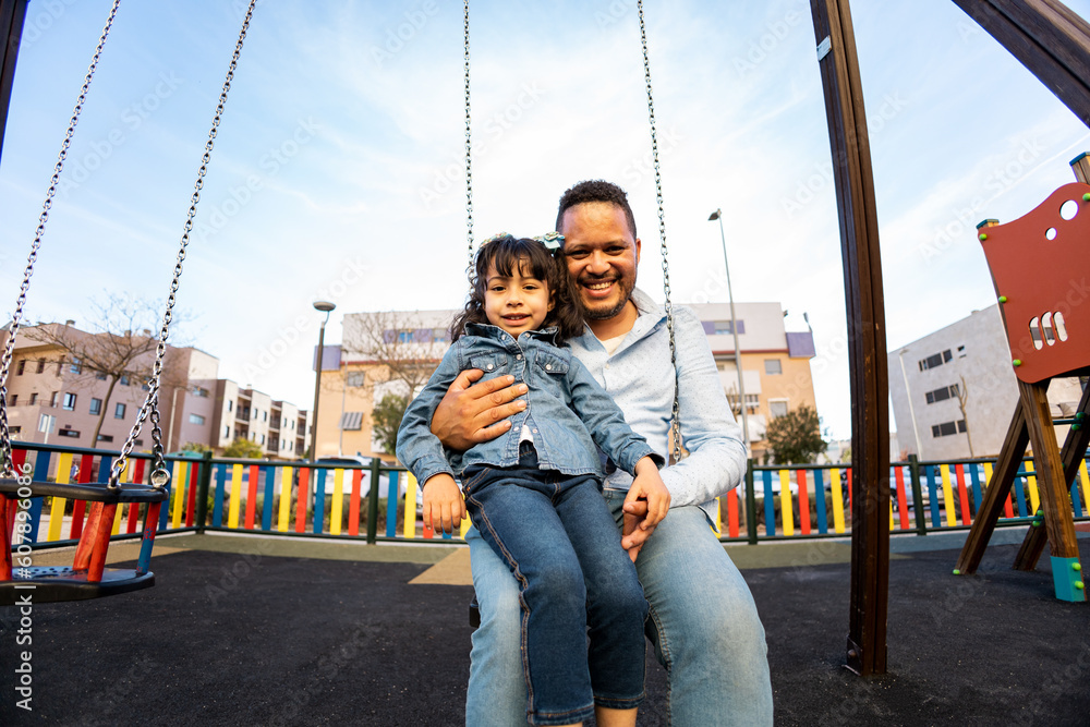 A dark-skinned father is playing with his daughter in an outdoor park ...