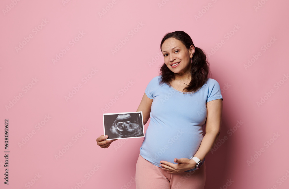 Pretty positive pregnant gravid woman smiles looking at camera, holds ...