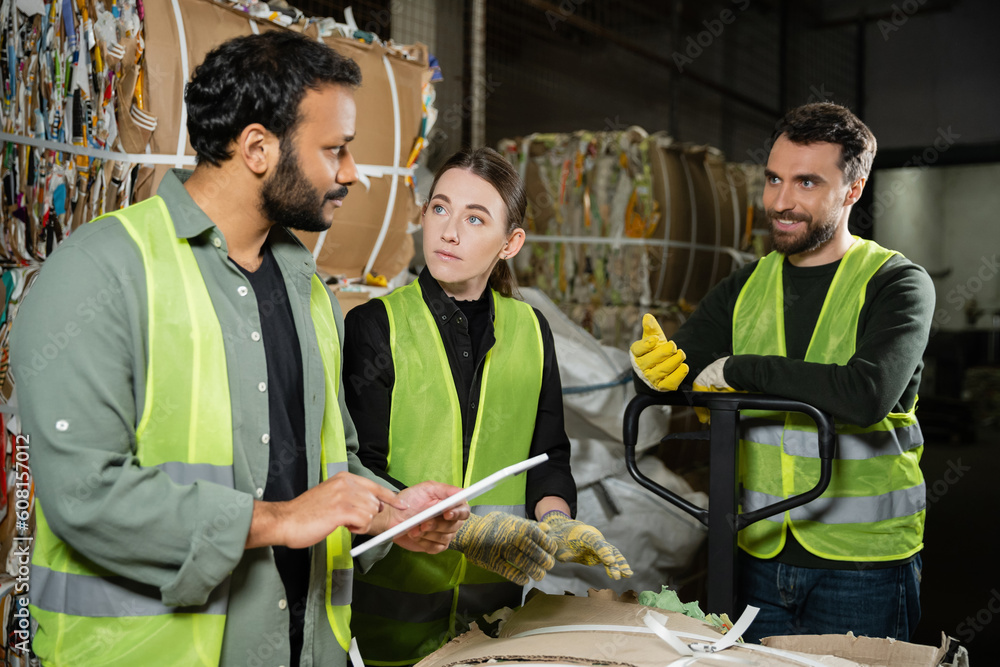 Smiling worker in reflective vest and gloves talking to multiethnic ...