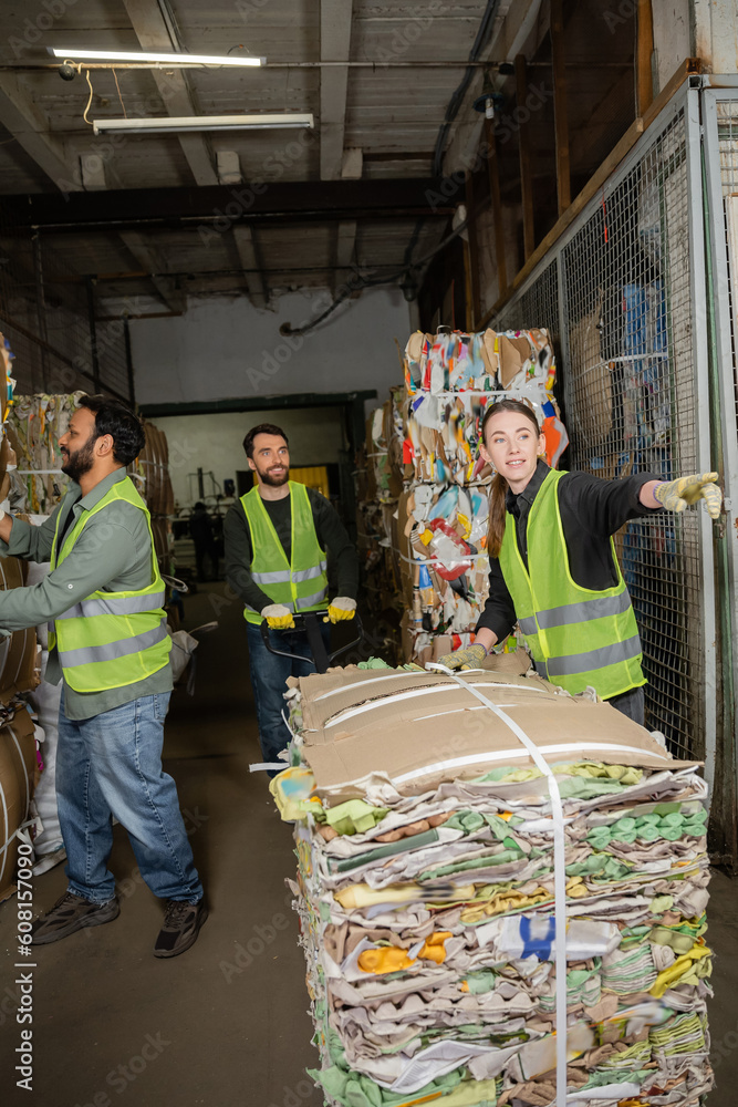 Smiling female worker in reflective vest and gloves pointing away while ...
