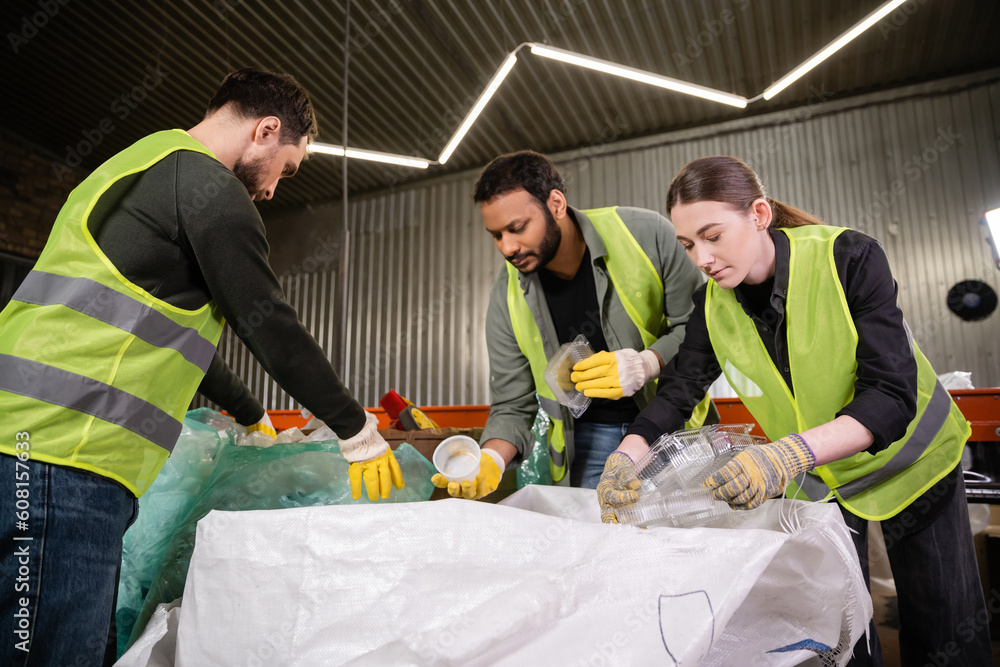 Young worker in reflective vest and gloves holding plastic containers ...
