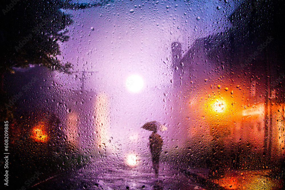 View through a glass window with raindrops on a blurred silhouette of a ...
