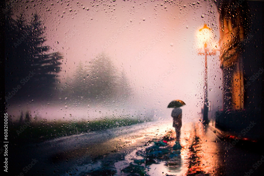 View through a glass window with raindrops on a blurred silhouette of a ...