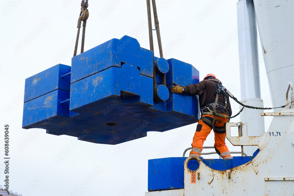 Worker in hi-vis and hard hat guides heavy steel counterweight into ...