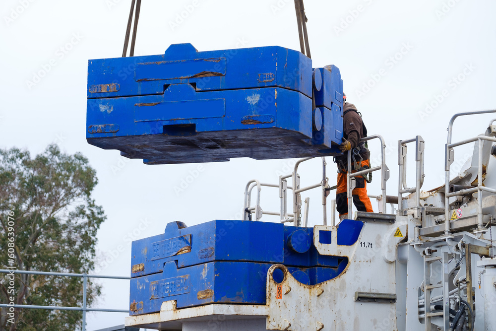 Worker in hi-vis and hard hat guides heavy steel counterweight into ...