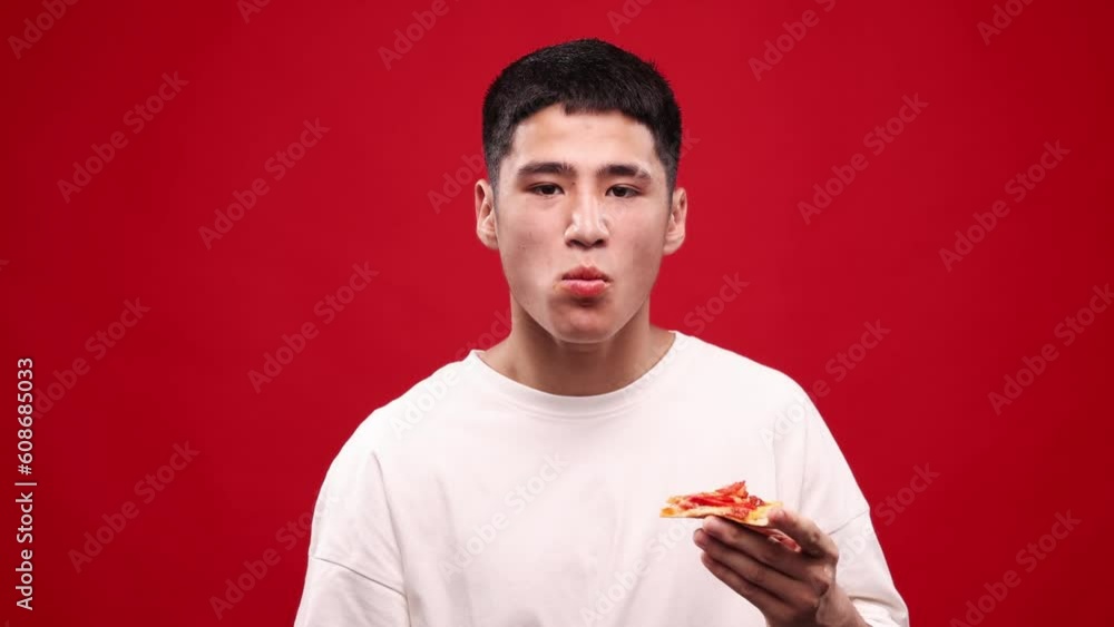 Spicy taste. Young asian guy eating slice of pizza with red chilli ...