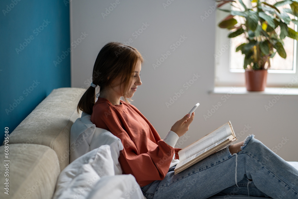 Addiction from phone. Interested smiling teen girl sit on bed with book ...