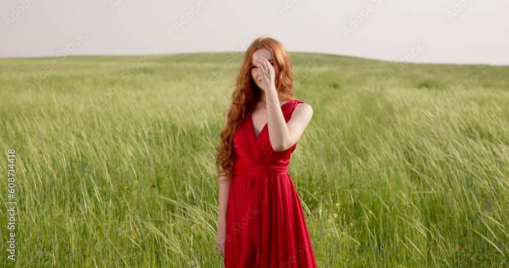 Woman with fiery hair stands in field at sunset with unwavering look ...