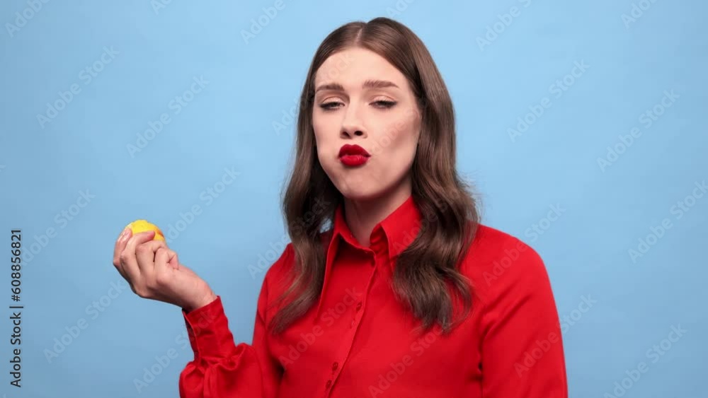 Young beautiful girl biting lemon against blue studio background ...