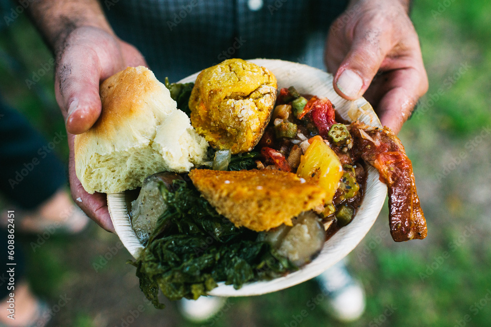 Foto de Hands hold a plate overloaded with food from a bbq including ...