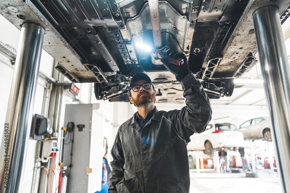 Auto mechanic with LED work light inspecting car chassis standing under ...
